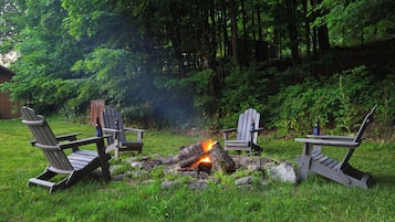 Um camping com três cadeiras Adirondack ao redor de uma fogueira.