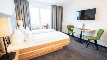 Quarto de hotel com cama, escrivaninha, duas cadeiras, televisão e varanda.
