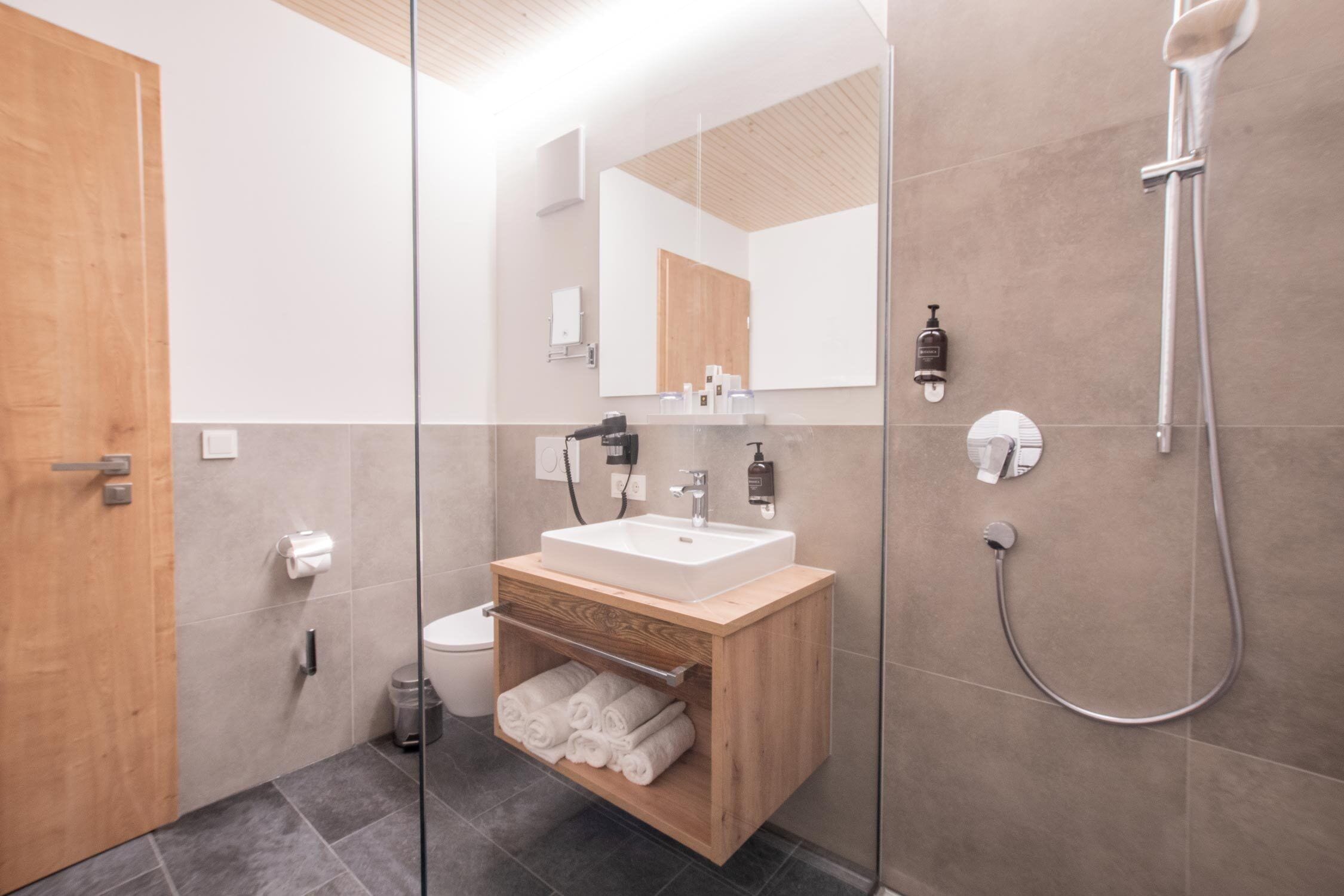 Um banheiro moderno com box de vidro, toucador de madeira e vaso sanitário.