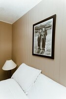 Quarto de hotel com uma cama, uma fotografia emoldurada na parede e um abajur.