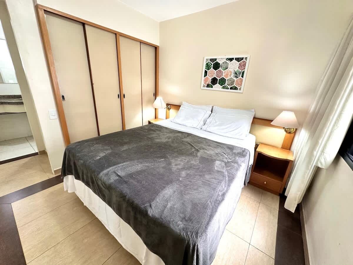 Quarto com cama, mesas de cabeceira, guarda-roupa e uma obra de arte na parede.