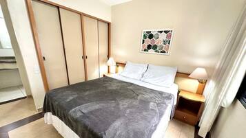 Quarto com cama, mesas de cabeceira, guarda-roupa e uma obra de arte na parede.