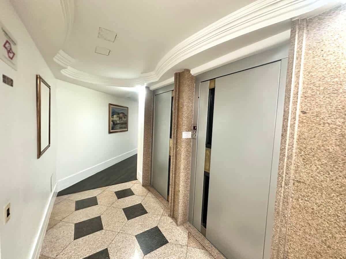 Um corredor com piso estampado, um quadro na parede e um elevador.