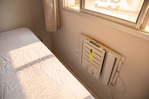 Uma cama de solteiro com colchão branco num quarto com janela.