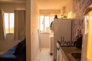 A compact kitchen with a gas stove, a refrigerator, and a window with curtains.