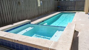 Piscina retangular com borda revestida, cercada por um muro de madeira e um espaço de pátio.