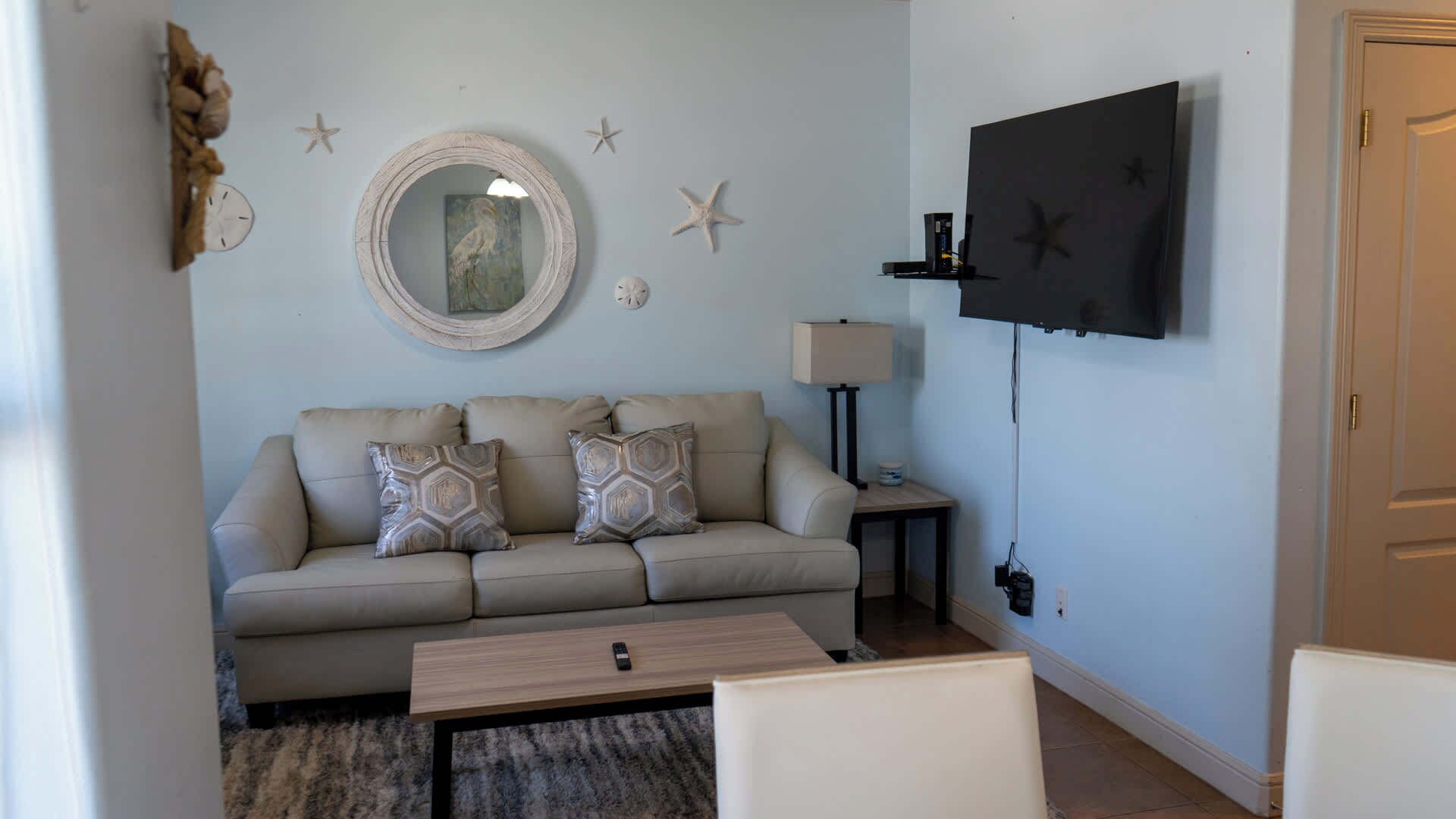 Uma sala de estar com sofá, mesa de centro, televisão e estrelas-do-mar decorativas na parede.