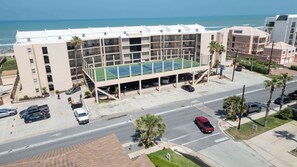 Um hotel com vários andares, quadra de tênis no terraço, estacionamento subterrâneo e vista para o oceano.