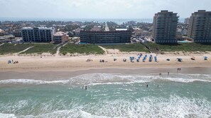 Uma praia com guarda-sóis e pessoas, um calçadão e edifícios ao fundo.