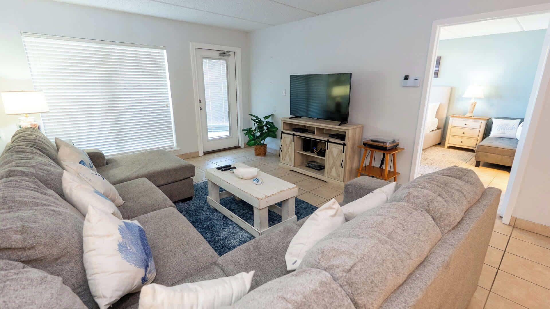 Uma sala de estar com sofá, mesa de centro, televisão e uma pequena mesinha lateral.
