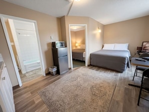 Quarto com cama, escrivaninha, cadeira, micro-ondas e lixeira.