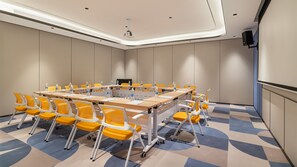Sala de conferência com uma grande mesa, cadeiras amarelas, garrafas de água e um projetor.