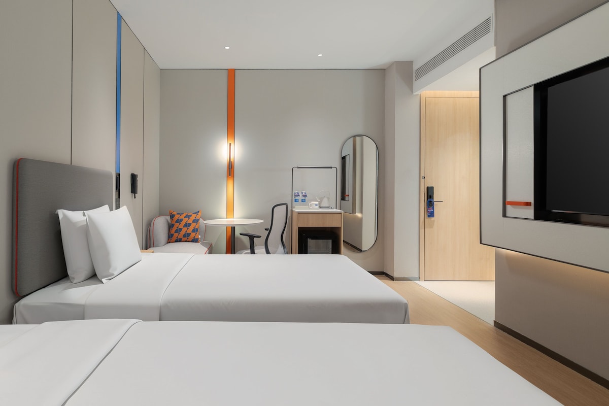 Quarto de hotel com duas camas, uma escrivaninha, uma cadeira, uma televisão e um espelho.