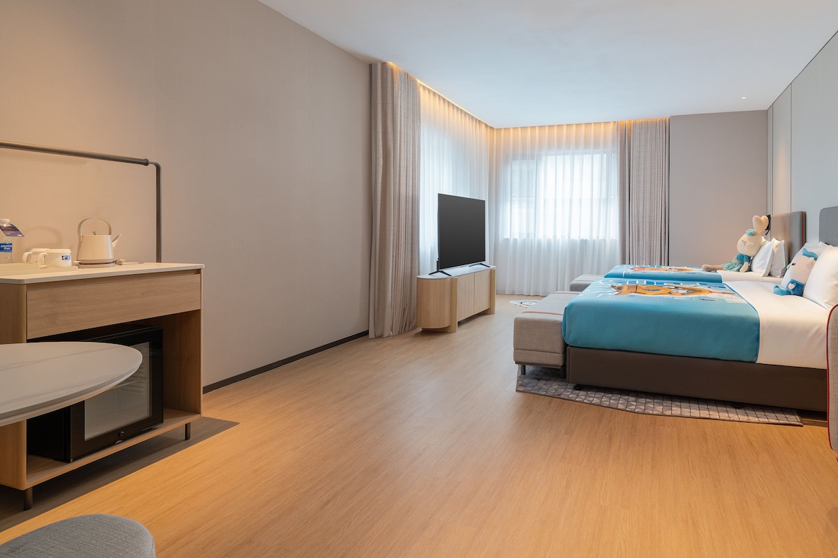 Quarto de hotel com cama, escrivaninha, televisão e área de estar.