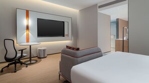 Quarto de hotel moderno com uma cama, escrivaninha, cadeira e televisão na parede.