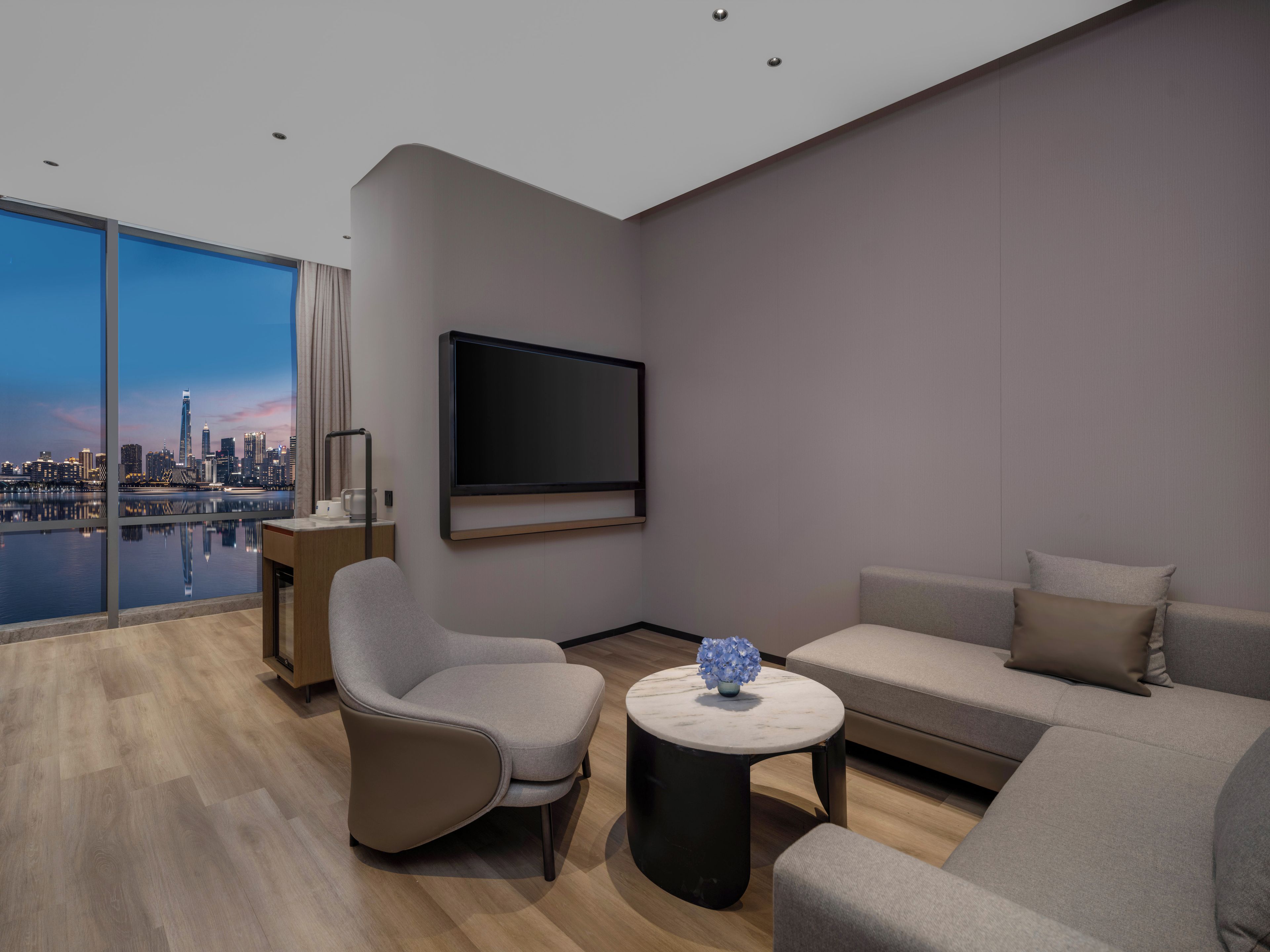 Quarto de hotel moderno com vista para o horizonte da cidade, TV de tela plana e um sofá.