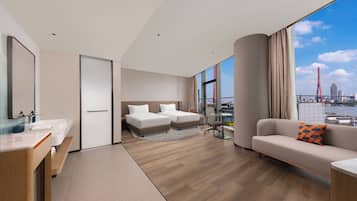 Quarto de hotel moderno com uma janela grande, um sofá, uma escrivaninha e duas camas.