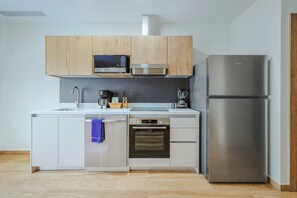 Uma cozinha moderna com armários brancos, uma geladeira de aço inoxidável, micro-ondas, forno Bosch e lava-louças.