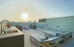 Um terraço no terraço com design moderno, incluindo uma pia, cadeiras de descanso e vista para o horizonte da cidade.