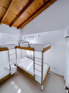 Um quarto com beliches, uma janela com cortinas e um aparelho de ar condicionado.