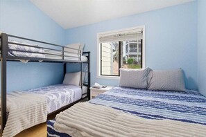 Quarto com beliches, janela com persianas e vista para um edifício.