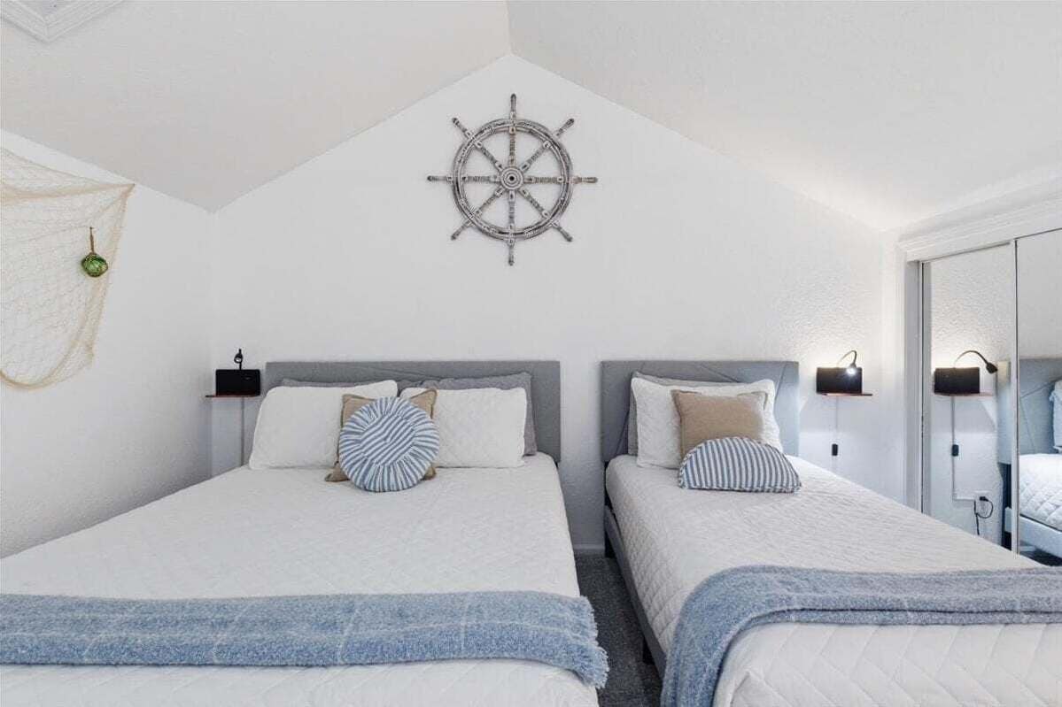 Quarto com duas camas, um adorno de leme e uma pequena decoração pendente.