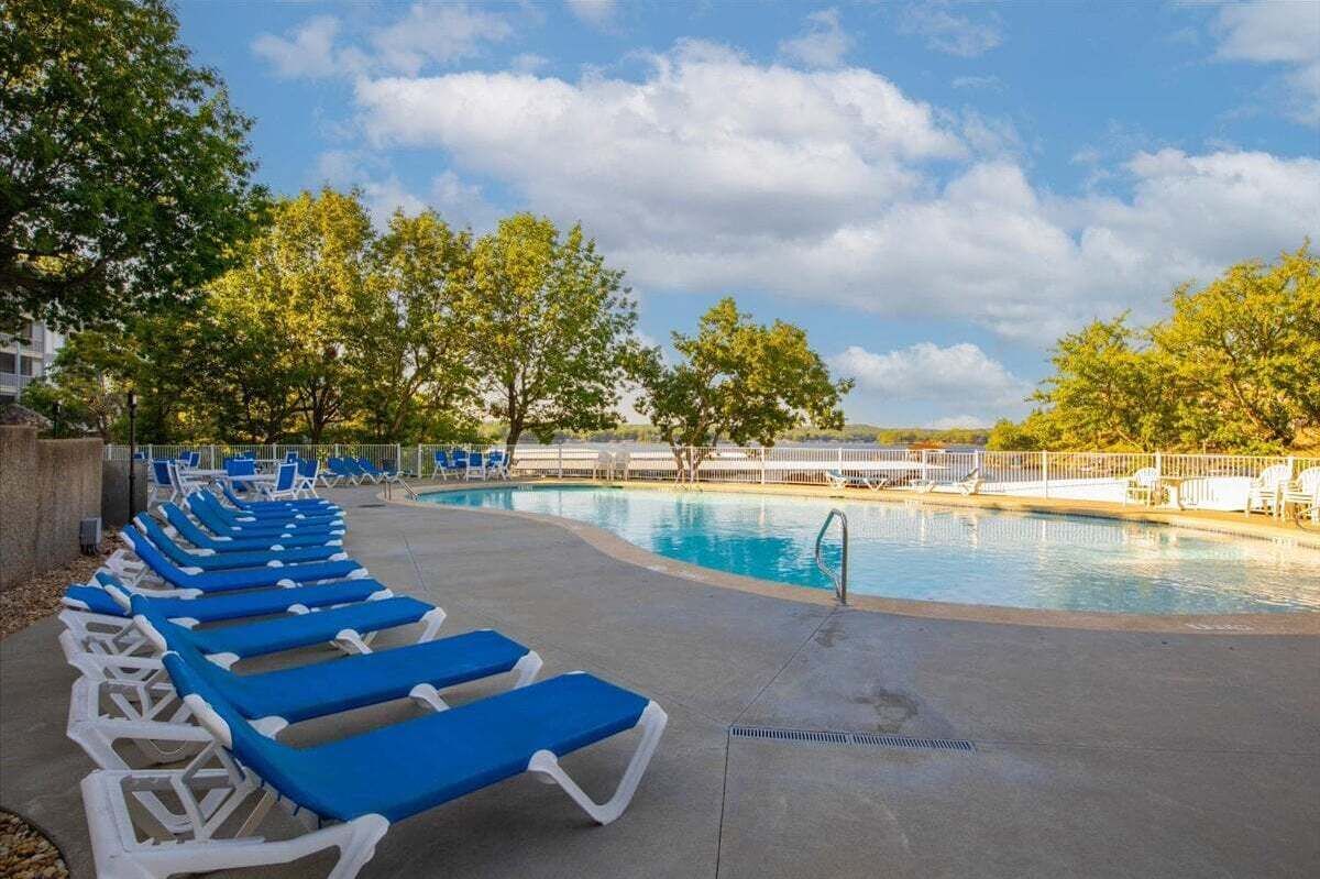 Área de piscina com espreguiçadeiras azuis e céu claro.