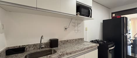 Uma cozinha com bancada de granito, pia de aço inoxidável, geladeira preta e micro-ondas sobre o fogão.