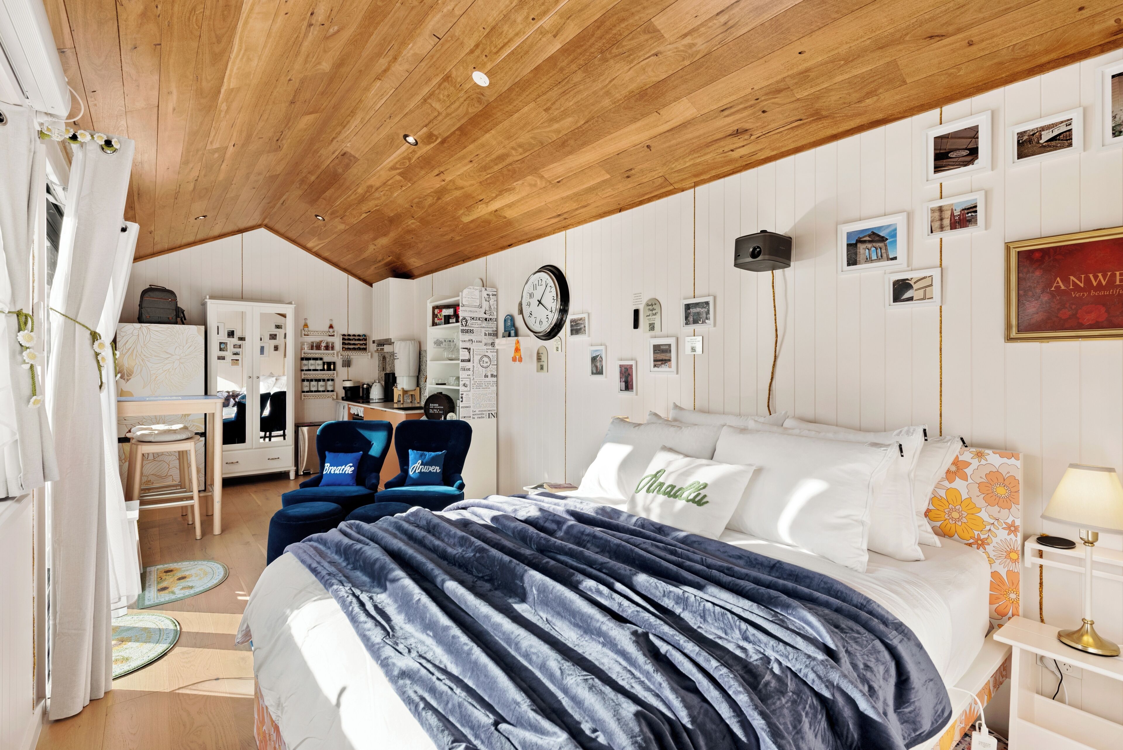Quarto com teto de madeira, cama com almofadas, escrivaninha e parede com quadros.