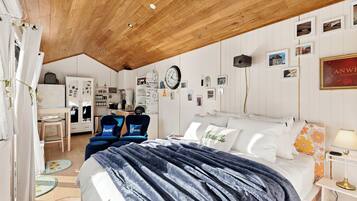 Quarto com teto de madeira, cama com almofadas, escrivaninha e parede com quadros.