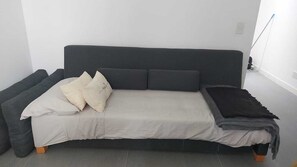 Um sofá escuro com uma almofada clara e um cobertor.