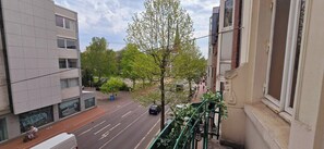 Vista da rua com um edifício moderno, uma avenida arborizada e um carro estacionado.