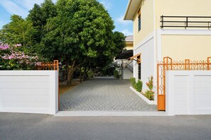 Uma entrada fechada por portão leva a um edifício com caminho de azulejos e uma árvore.