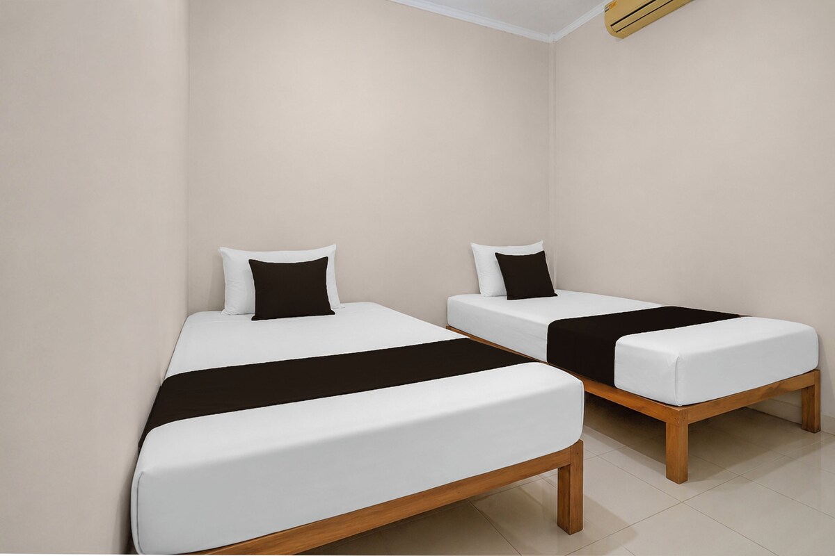 Quarto com duas camas de solteiro, cada uma com colchão branco e roupa de cama preta.