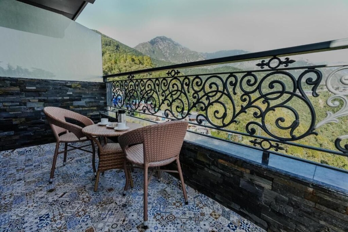 Uma varanda com cadeiras de vime, uma mesa e vista para as montanhas.