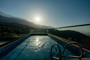 Piscina ao ar livre com vista para montanhas e o sol.
