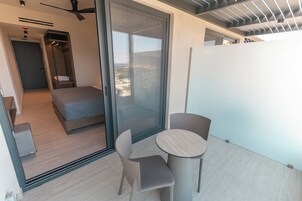 Um quarto moderno com uma cama, uma porta de correr de vidro e uma pequena varanda com mesa e cadeiras.