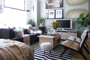 Uma sala de estar moderna com sofá, mesa de centro e poltrona, uma TV de tela plana e plantas decorativas.