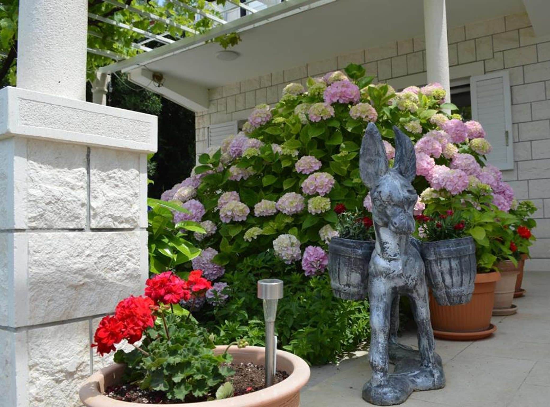 Um jardim com uma estátua, plantas em vasos e a fachada de um edifício.