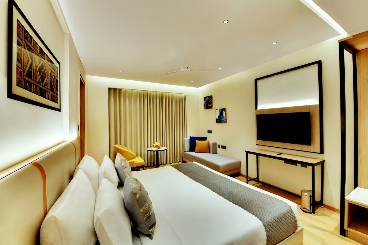 Quarto de hotel moderno com cama, televisão, escrivaninha e área de estar.