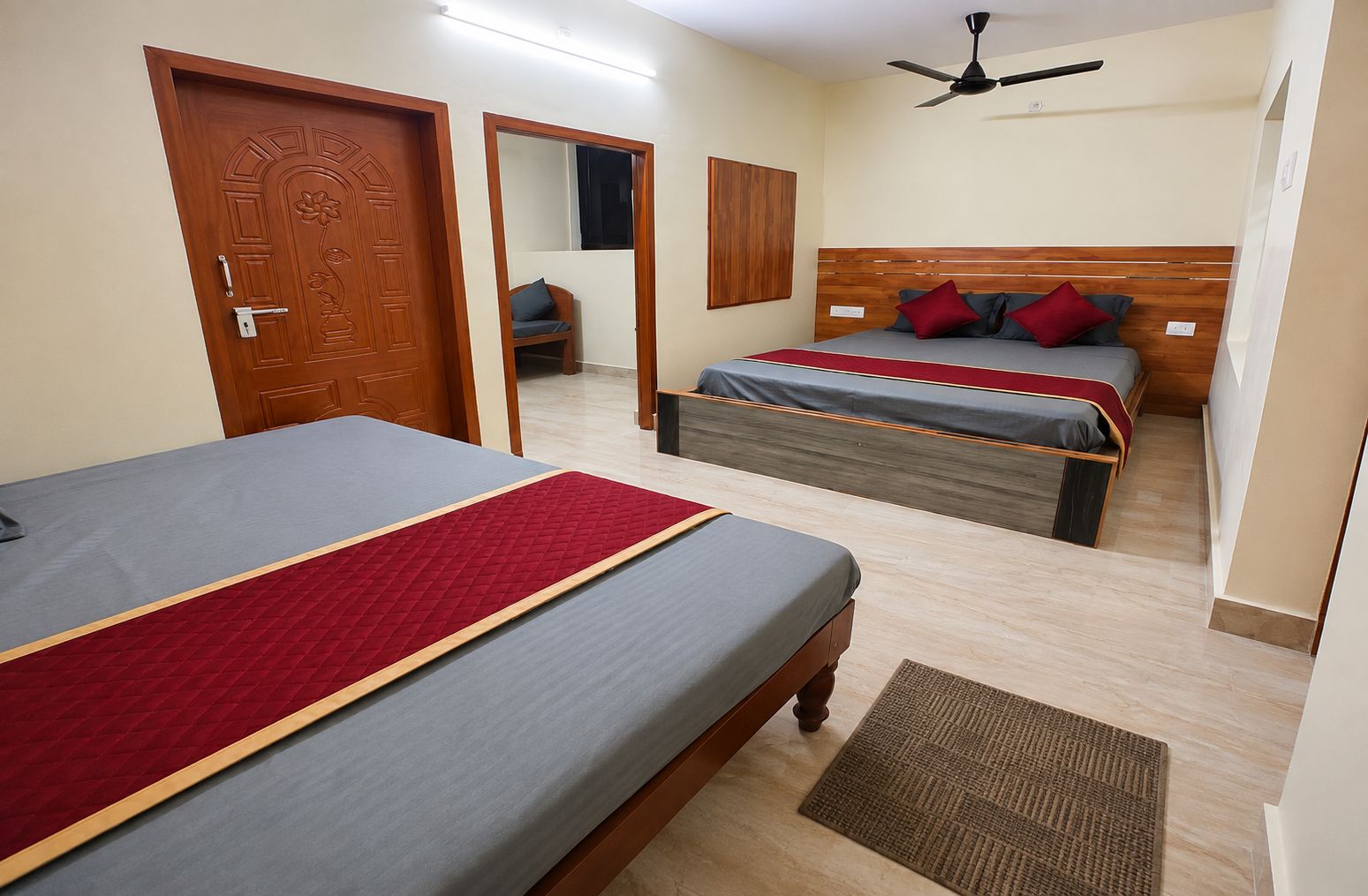 Quarto de hotel com duas camas, porta de madeira, ventilador de teto e espelho.