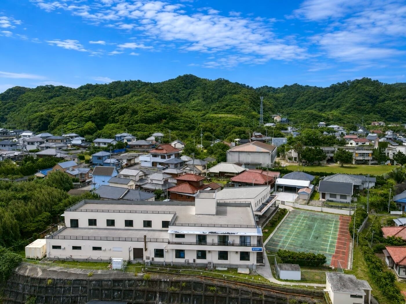 Um bairro residencial com casas, um campo esportivo e uma colina ao fundo.