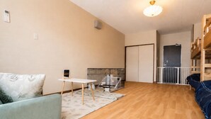 Quarto com piso de madeira, um sofá, uma mesinha com espelho, um berço e uma porta que dá para outro cômodo.