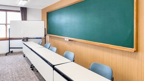 Uma sala de aula com um quadro negro grande, um quadro branco e uma longa mesa com cadeiras.