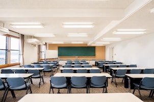 Uma sala de aula com fileiras de mesas e cadeiras, um quadro negro grande e um quadro branco.