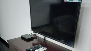 Uma mesa de madeira escura com uma televisão de tela plana, um controle remoto preto e outro branco, e um pequeno dispositivo preto sobre ela.