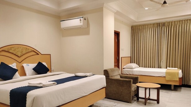 Quarto de hotel com duas camas, uma cadeira, uma mesinha, unidade de ar condicionado e ventoinha no teto.