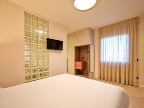 Quarto de hotel com uma cama grande, televisão na parede, guarda-roupa e janela com cortinas.