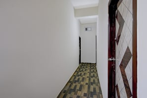 Um corredor com piso xadrez, paredes brancas e uma porta com padrão geométrico.