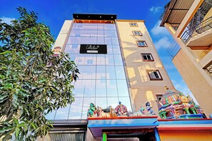 Um hotel com fachada moderna, uma placa indicando que é um conjunto de serviços corporativos, e uma estátua colorida de divindades no nível térreo.